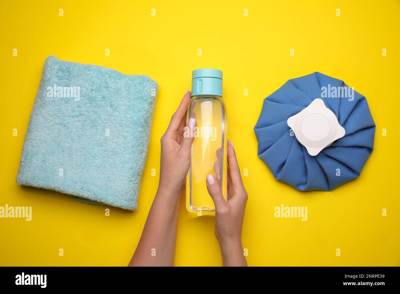 Woman with bottle of water, cold compress and towel on yellow ...