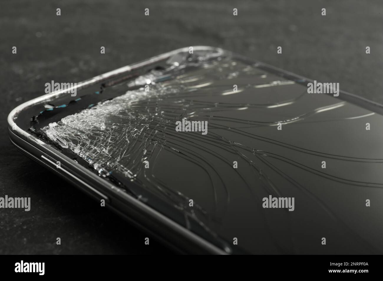 Smartphone with cracked screen on black table, closeup. Device repair ...