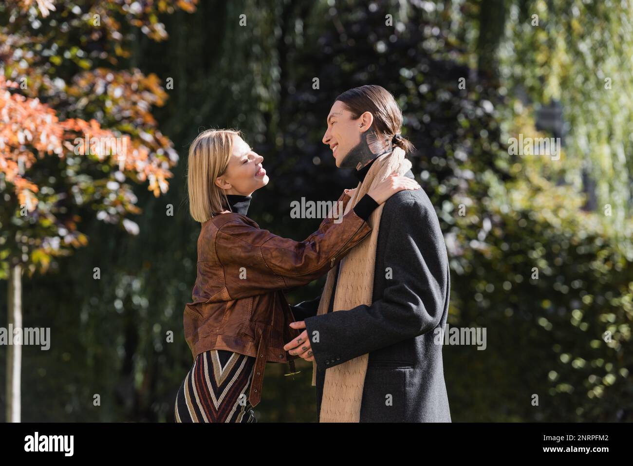 side view of happy blonde woman hugging tattooed boyfriend during date ...