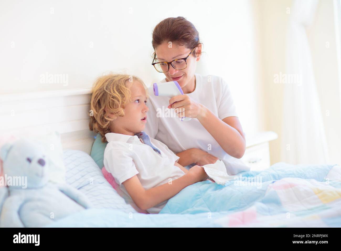 Sick child in bed. Mother checking on unwell kid. Little boy having fever feeling ill. Mom with ...