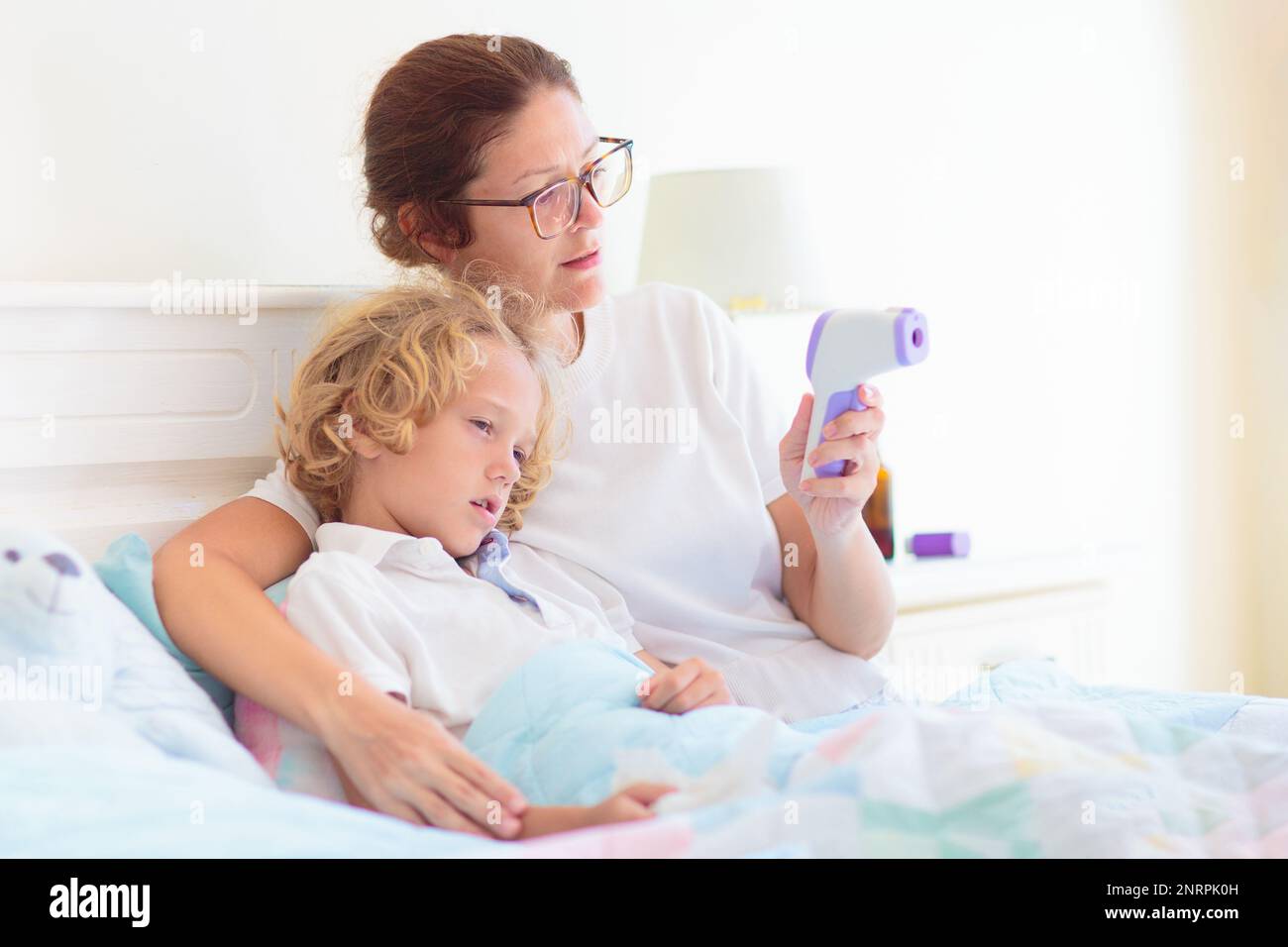 Sick child in bed. Mother checking on unwell kid. Little boy having fever feeling ill. Mom with ...