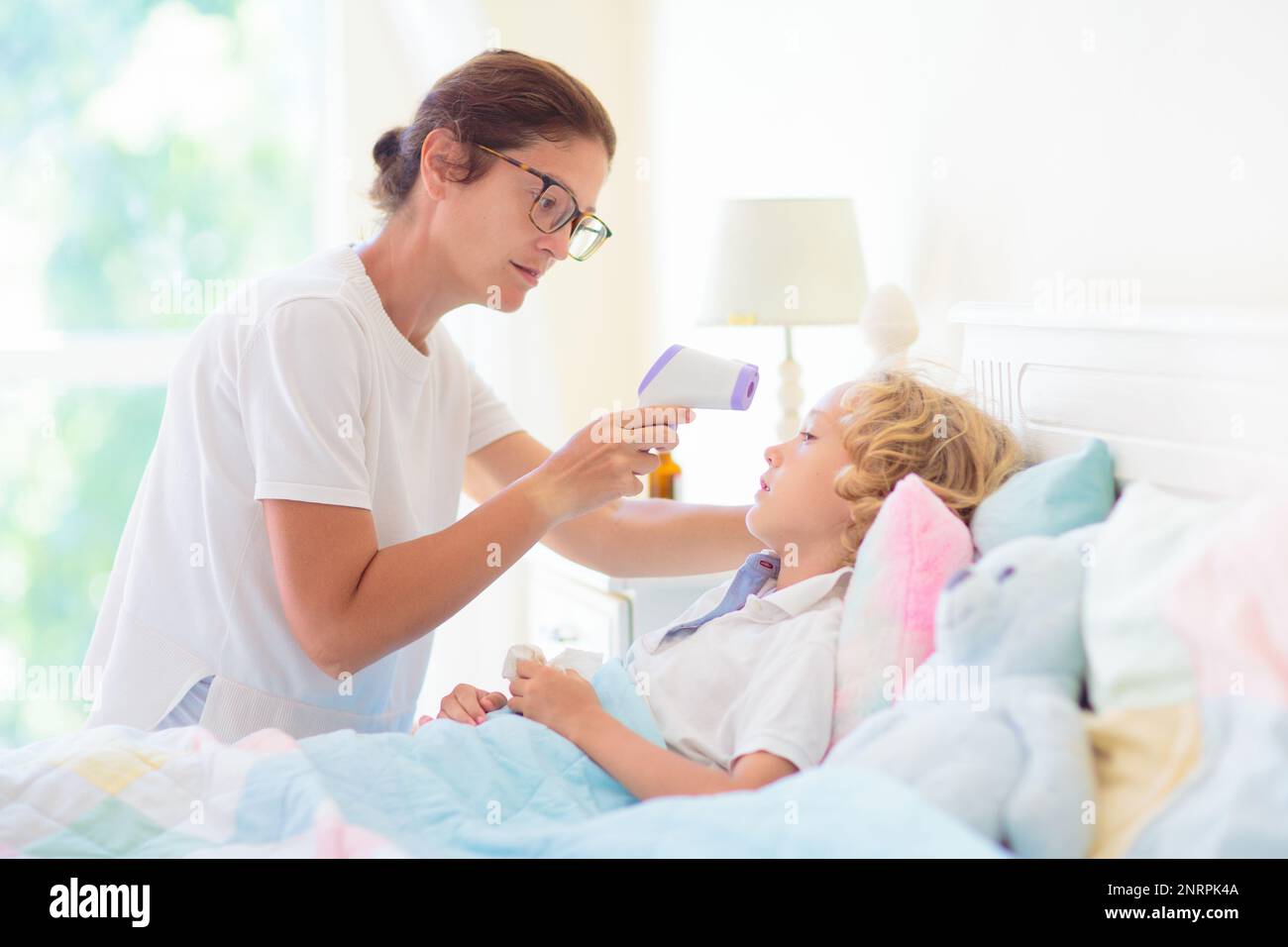 Sick child in bed. Mother checking on unwell kid. Little boy having fever feeling ill. Mom with ...