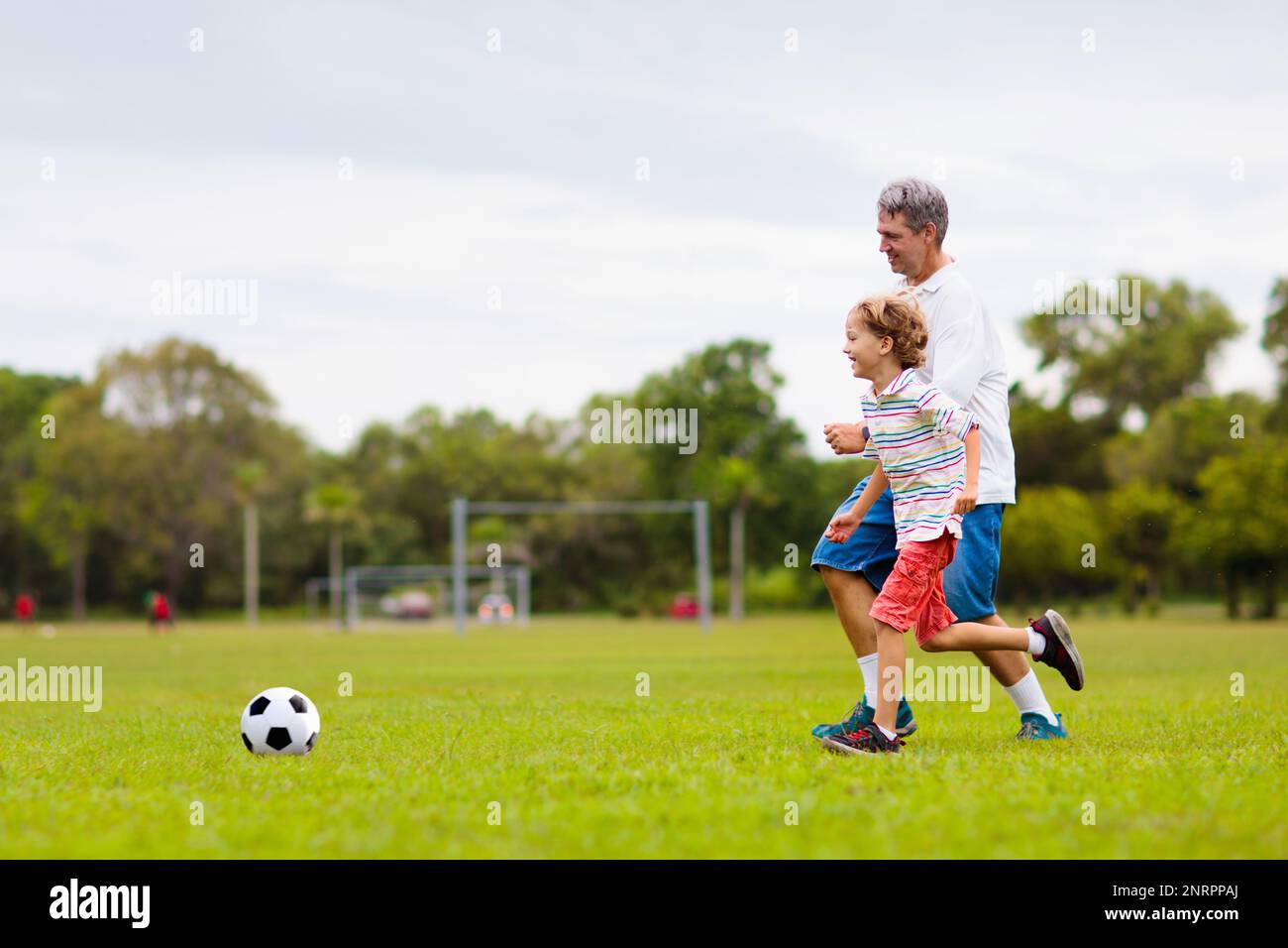 Father and son play football on outdoor pitch. Dad and kid run on park ...