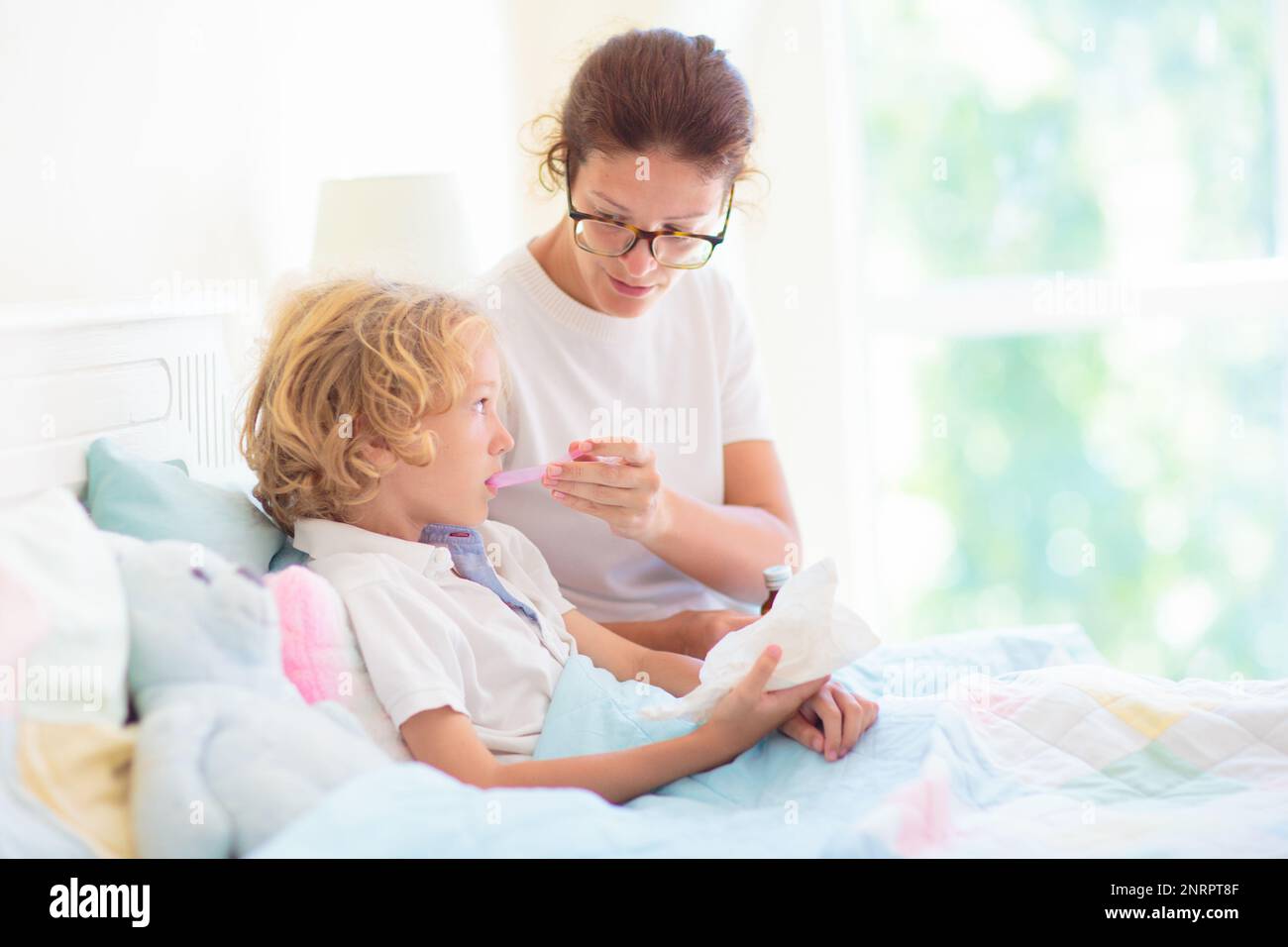 Sick child in bed. Mother checking on unwell kid. Little boy having fever feeling ill. Mom with ...