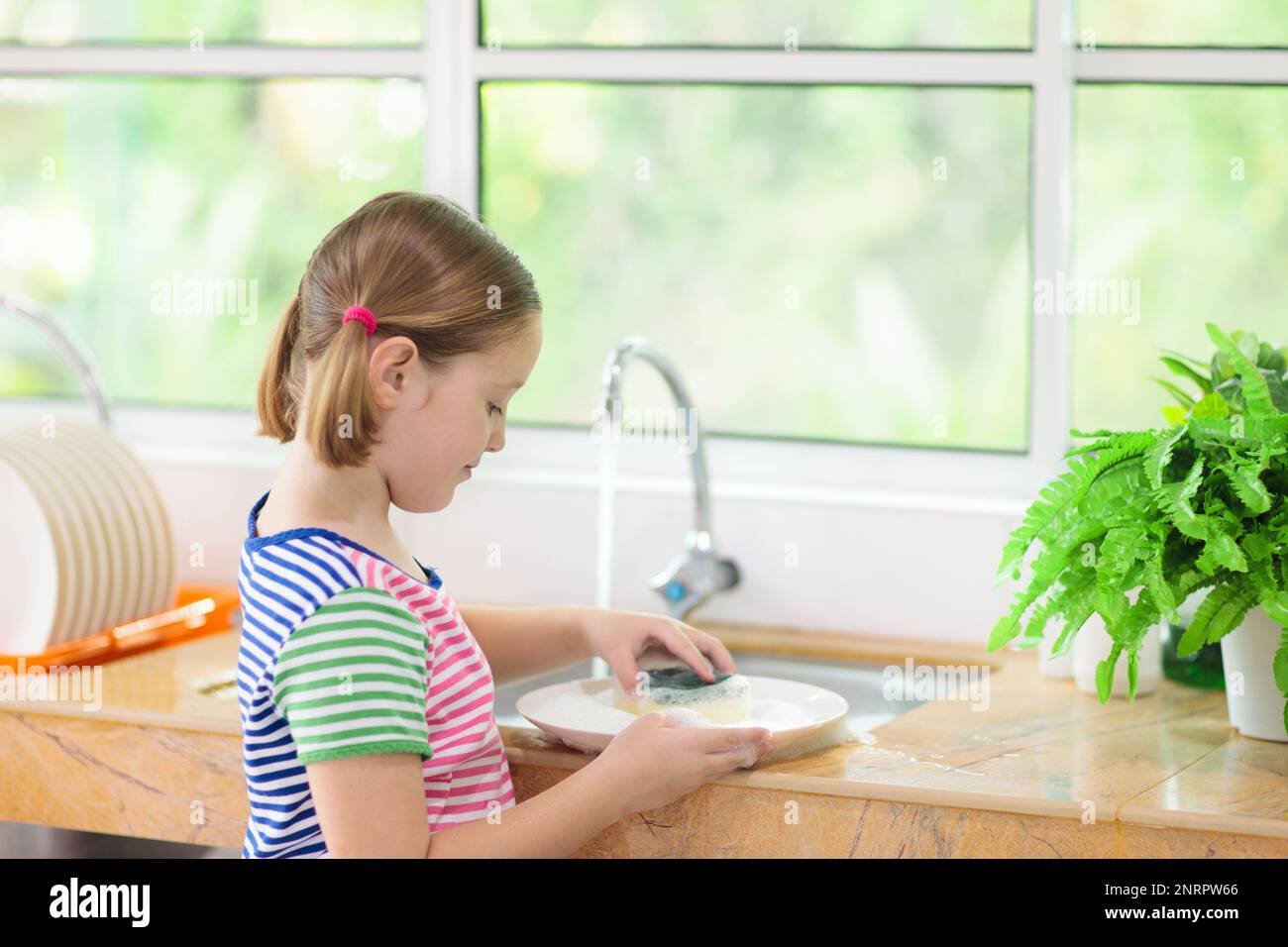 Child washing dishes. Home chores. Kid in white kitchen cleaning plates ...