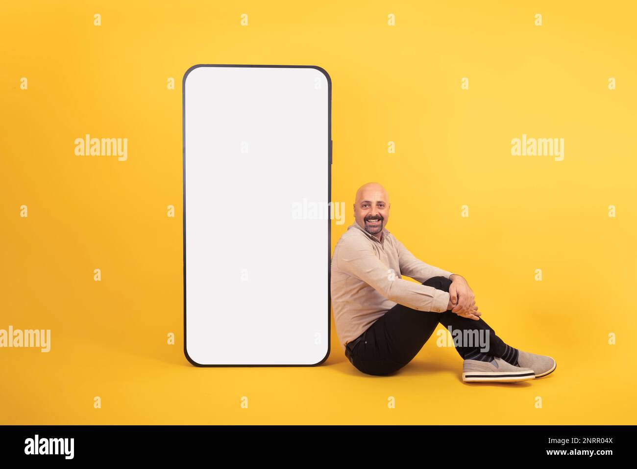 Full size caucasian male sitting near big mobile cell phone with blank ...