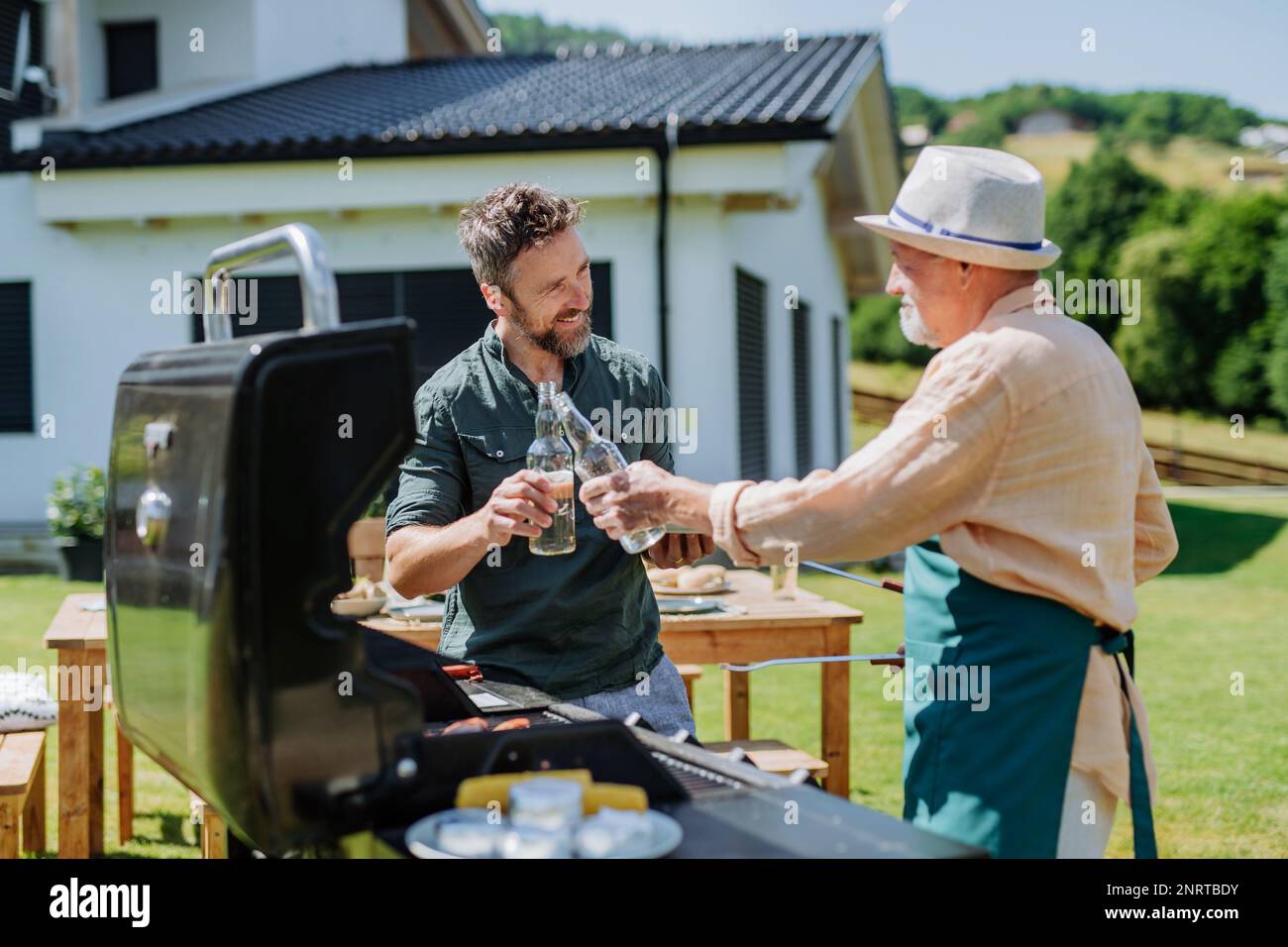 Senior father with adult son grilling outside on backyard in summer ...