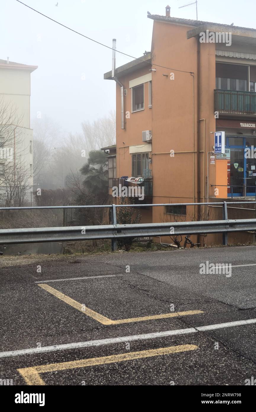 Stream of water between buildings seen from a road on a foggy day in ...