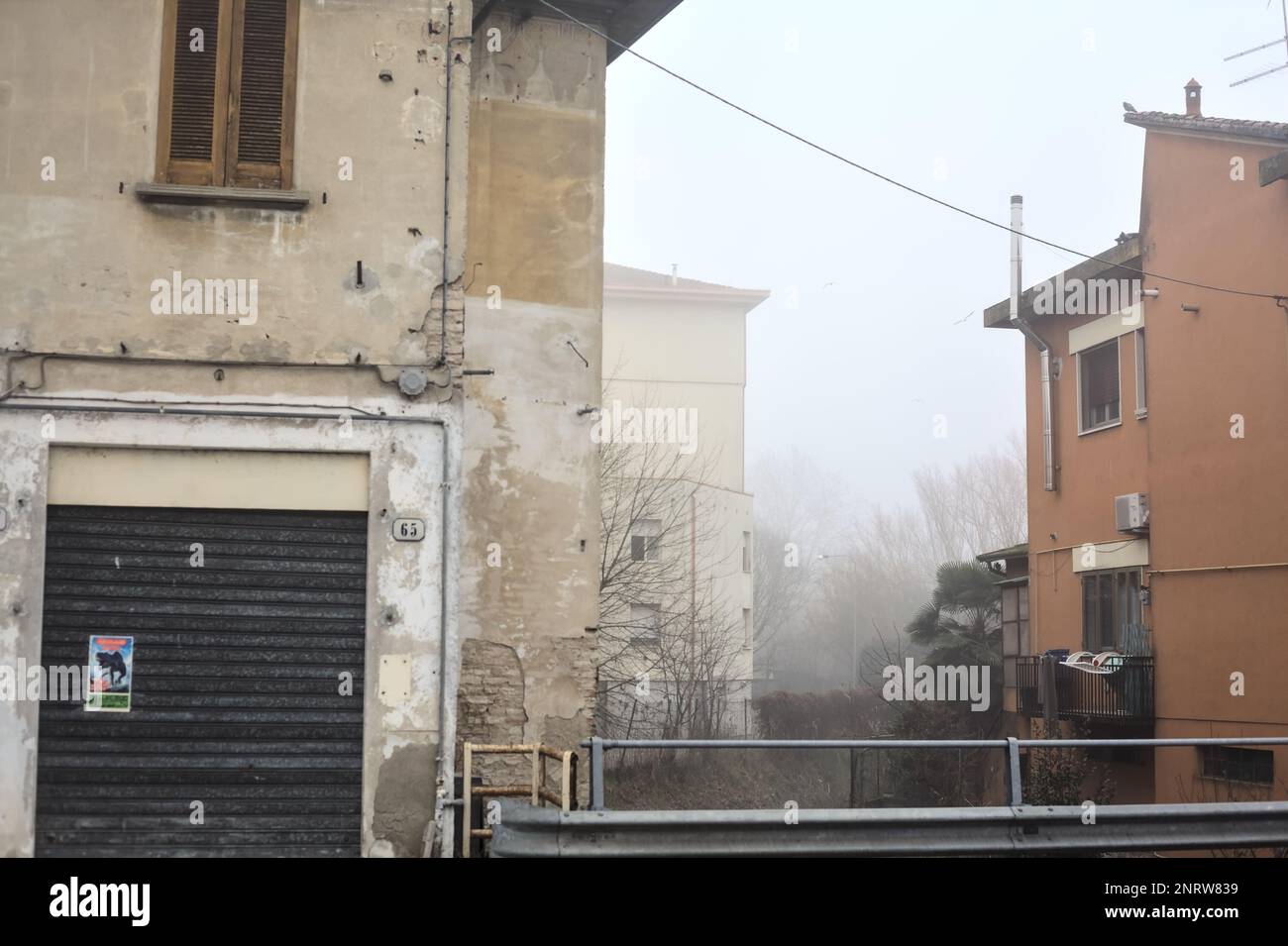 Stream of water between buildings seen from a road on a foggy day in ...