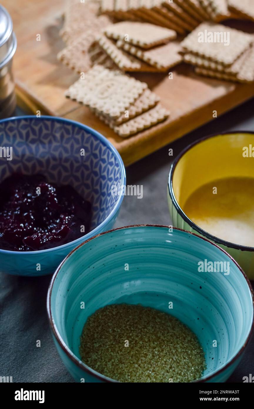 bowls with sugar, melted butter, jam and biscuits on a cutting board to ...