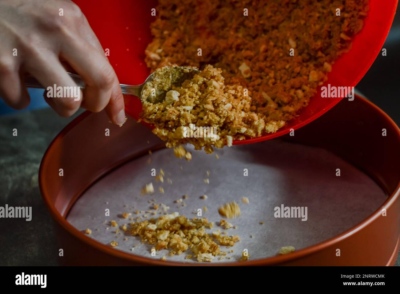 hands pouring the mix of biscuit crumbs, sugar and butter into the pan ...