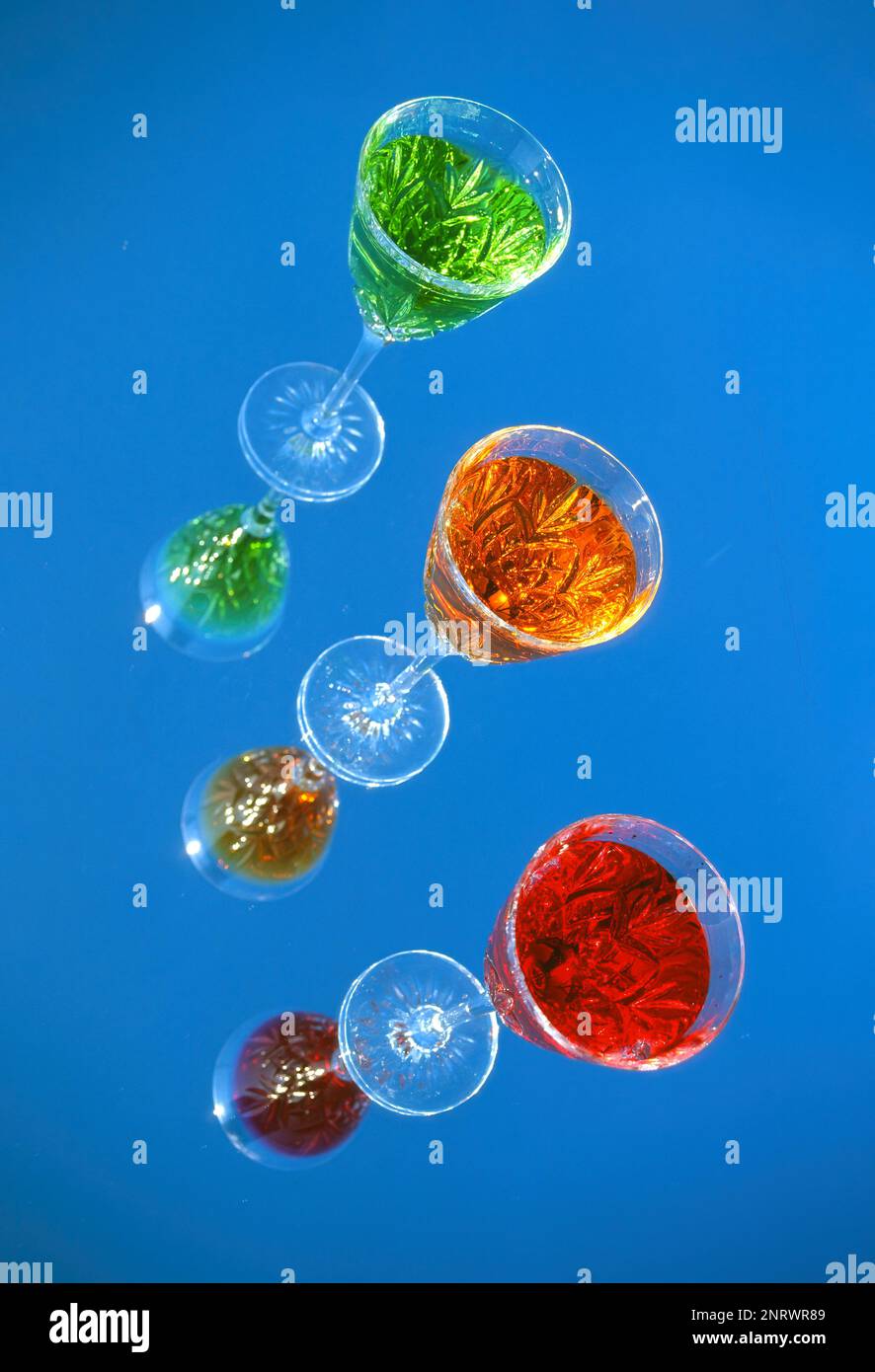 Three glasses with coloured liquid taken on a mirror with blue sky ...