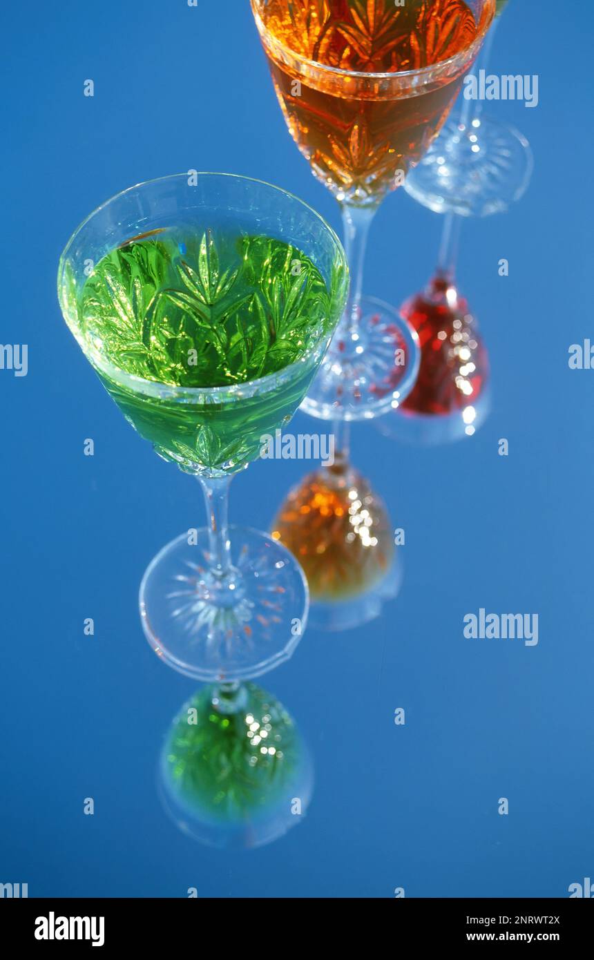 Three glasses with coloured liquid taken on a mirror with blue sky ...