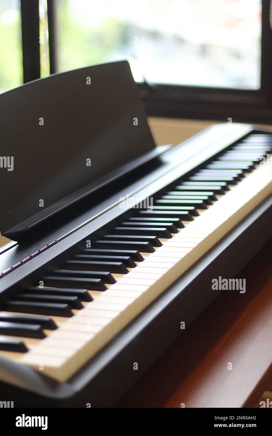 Black piano keyboard with white keys against window interior background ...