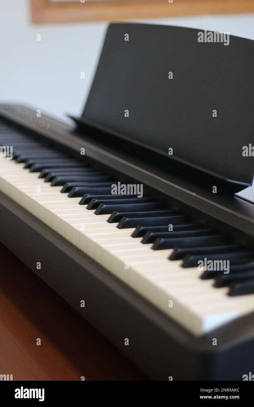 Black piano keyboard with white keys against window interior background ...