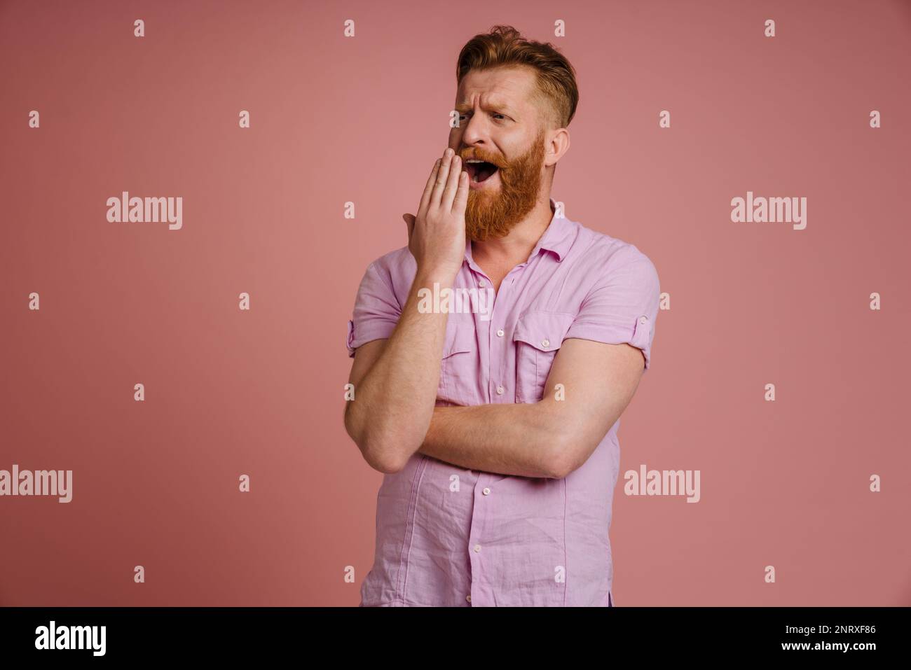 Ginger white man with beard yawning while covering his mouth isolated ...