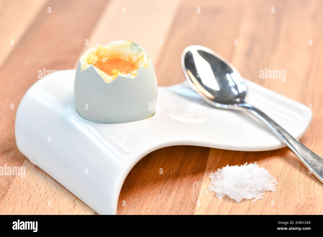 a single boiled egg in an egg cup broken open showing yolk with a spoon ...