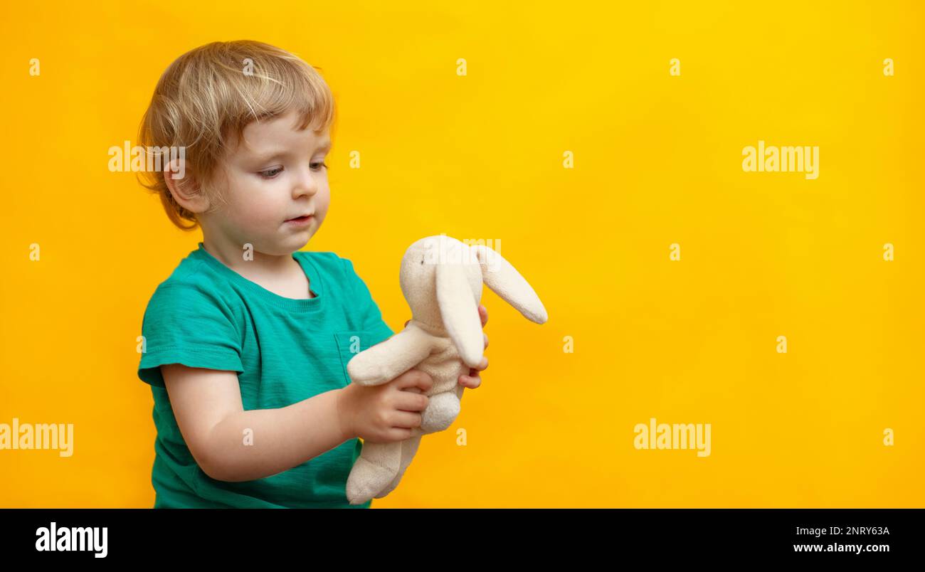 Cute little kid hugging a plush rabbit bunny toy on yellow background ...