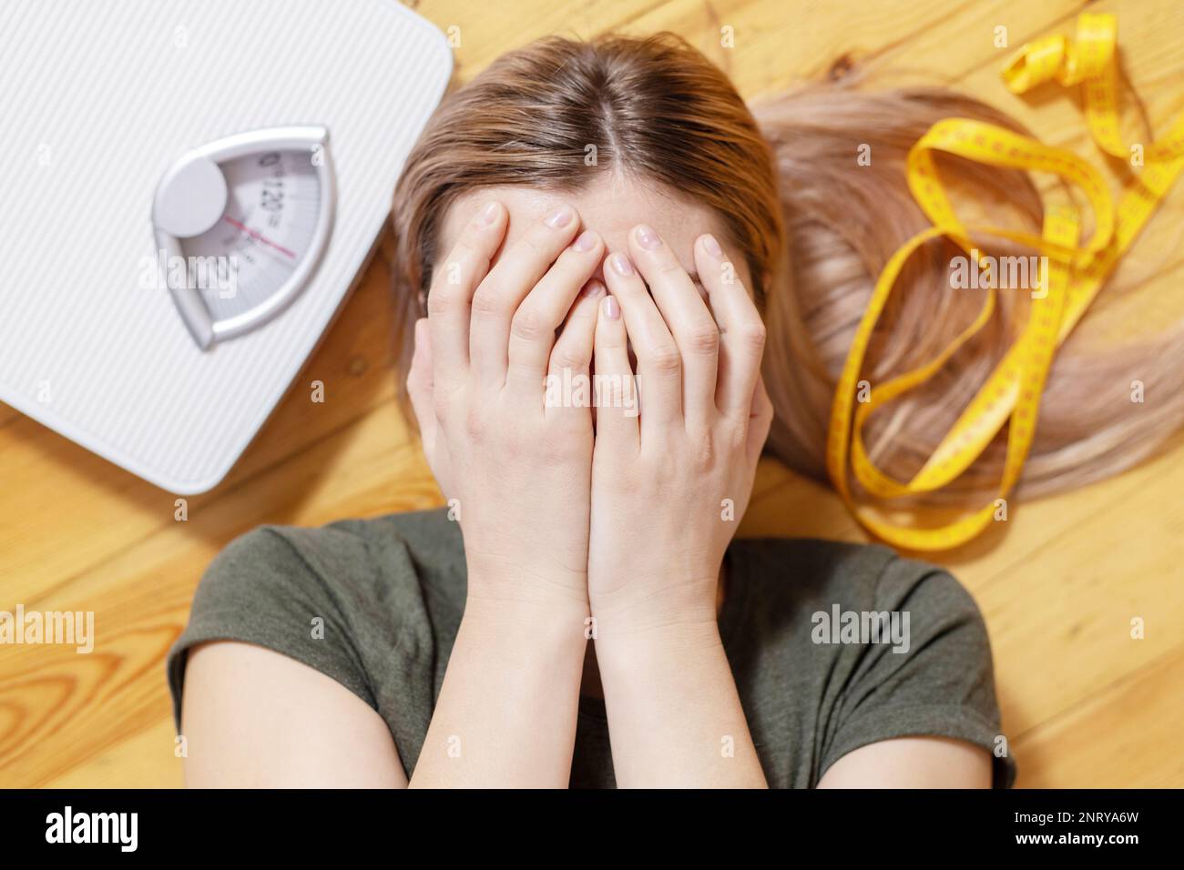 Sad woman lying on wooden floor with white scales and measuring tape ...