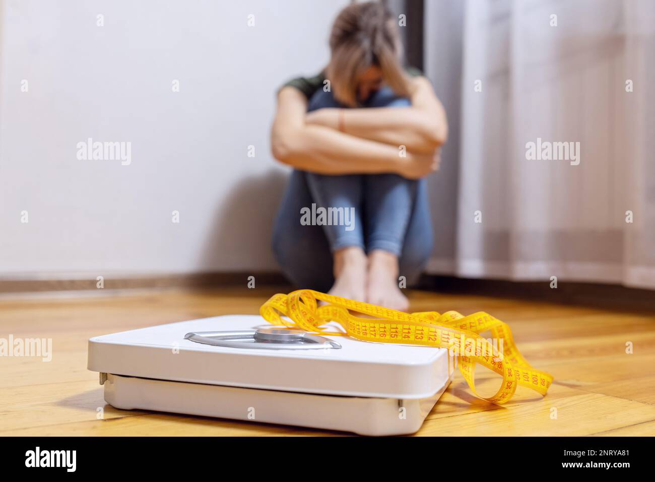 White scale and upset, sad woman with measuring tape on wooden floor ...