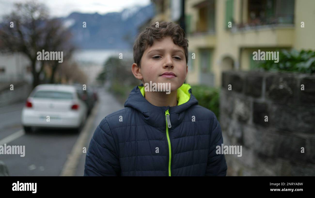 One pensive young boy walking in city street forward. Preteen male kid ...