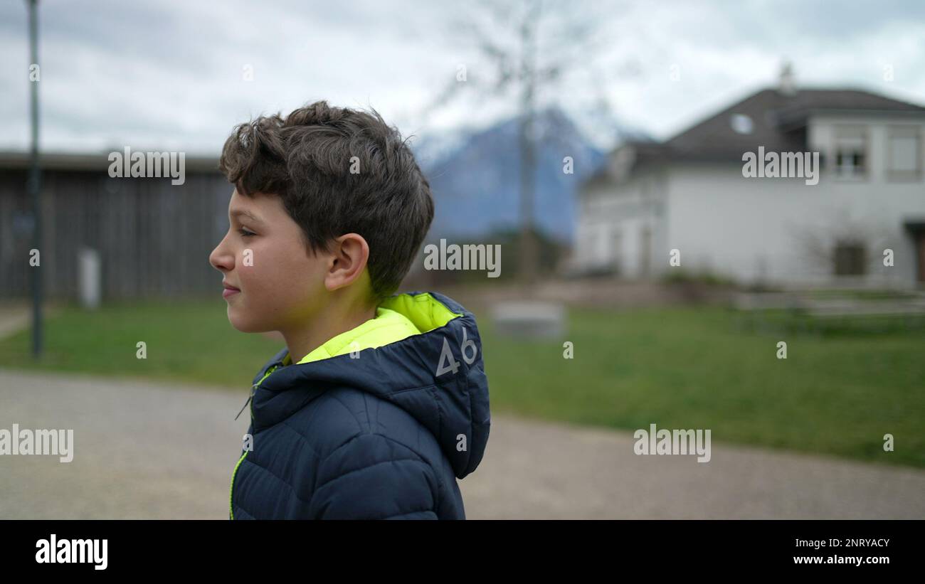 One pensive young boy walking forward outside at park. A contemplative ...