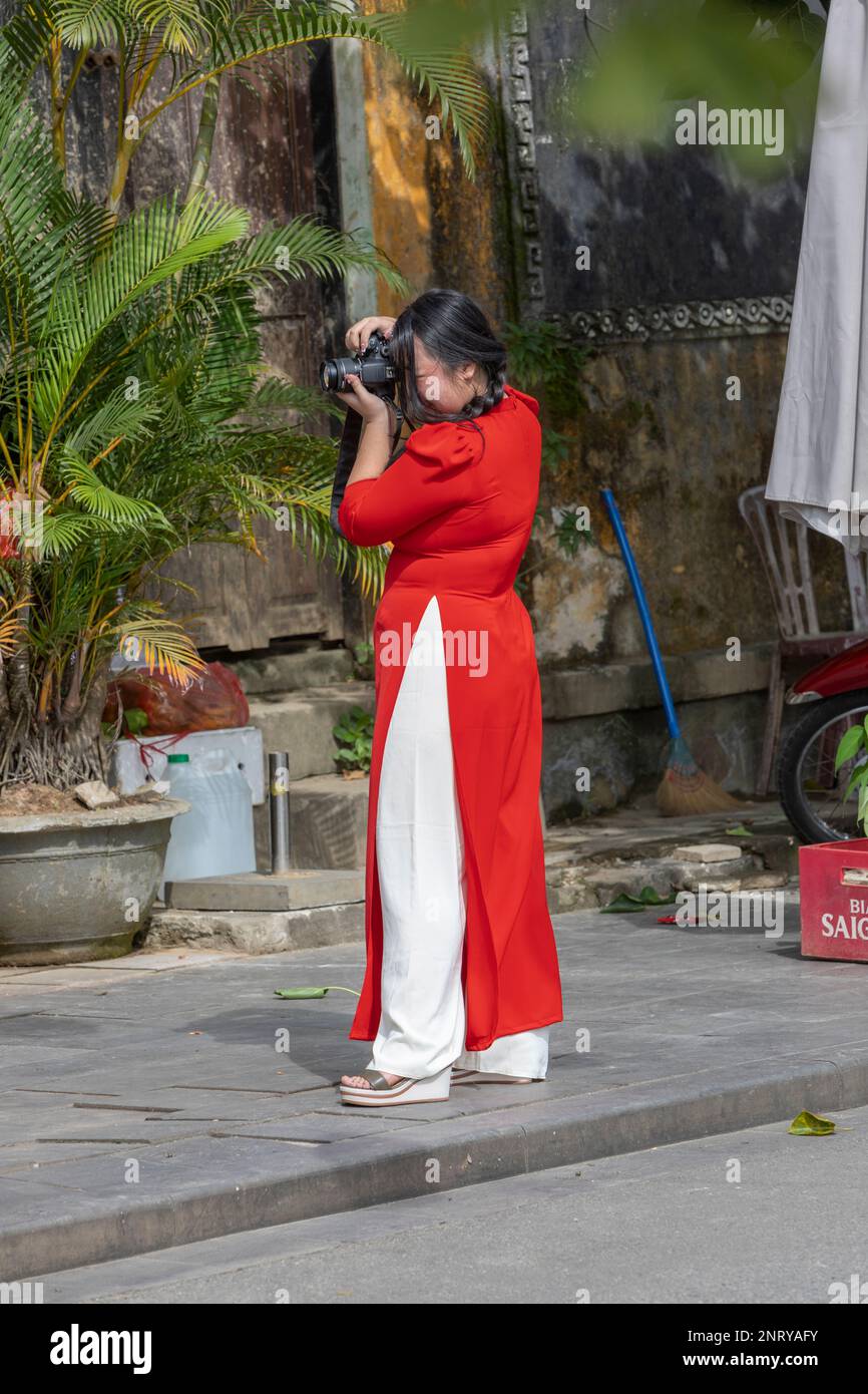 A vietnamese lady in traditional dress taking photographs in the street ...