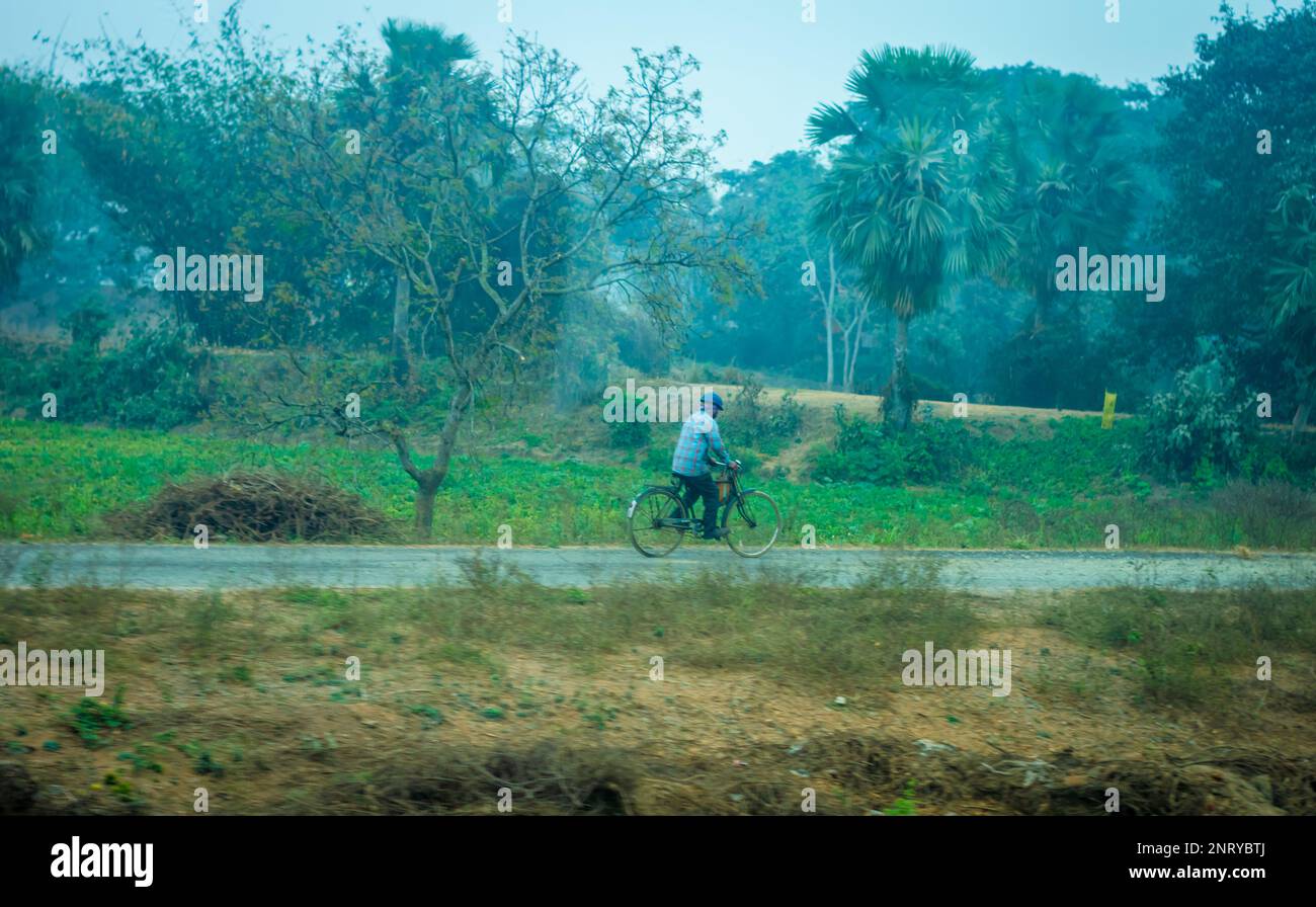 A man riding bycle on a village road in rural background. Photography ...