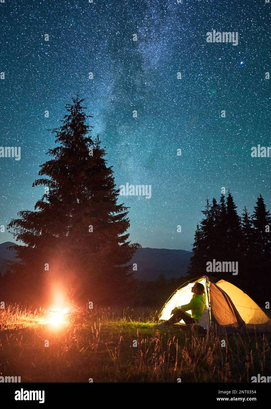 Night camping in mountains under starry sky and Milky way. Female tourist sitting in tent ...