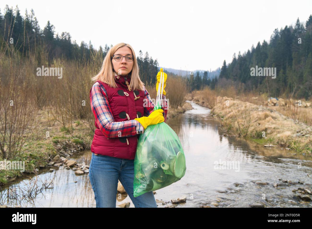 Blond hair woman in glasses collecting plastic garbage near the river ...