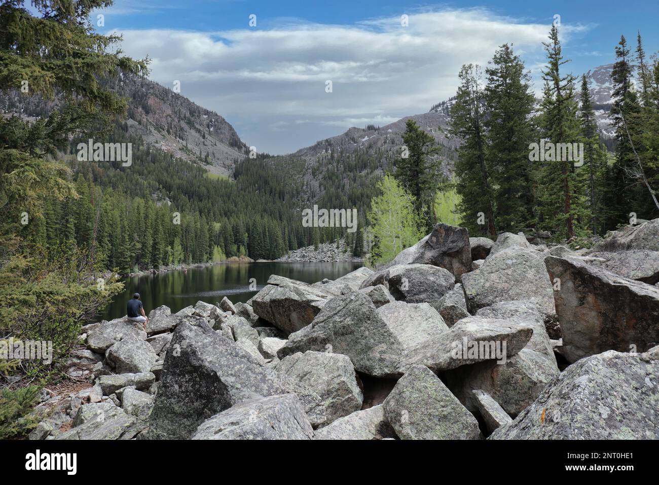 A young man sitting on a boulder looking at Weller Lake, surrounded ...