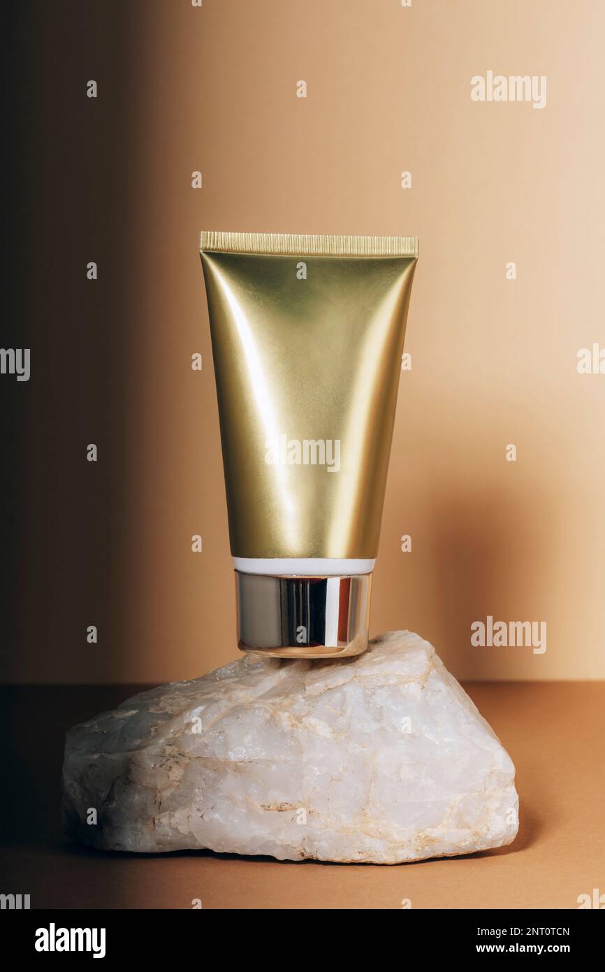 Golden cream tube on natural podium stand. Skin care, beauty and spa ...