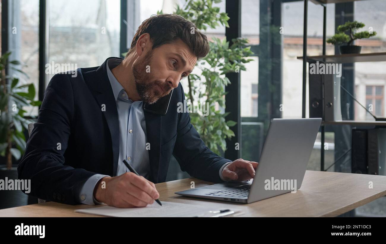 Busy successful caucasian adult businessman in office typing on laptop talking to client on ...