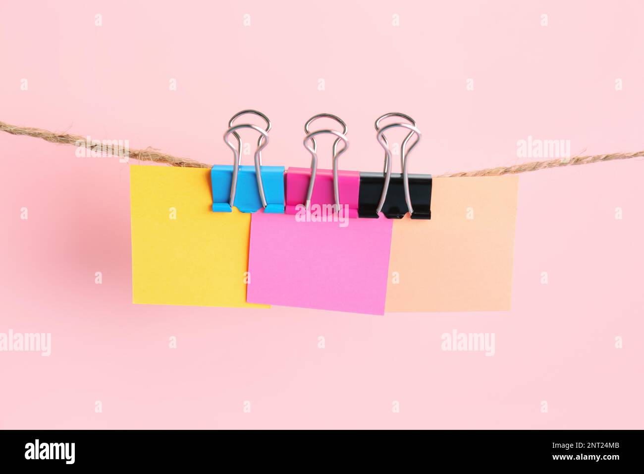 Sticky notes with binder clips hanging on rope against pink background ...