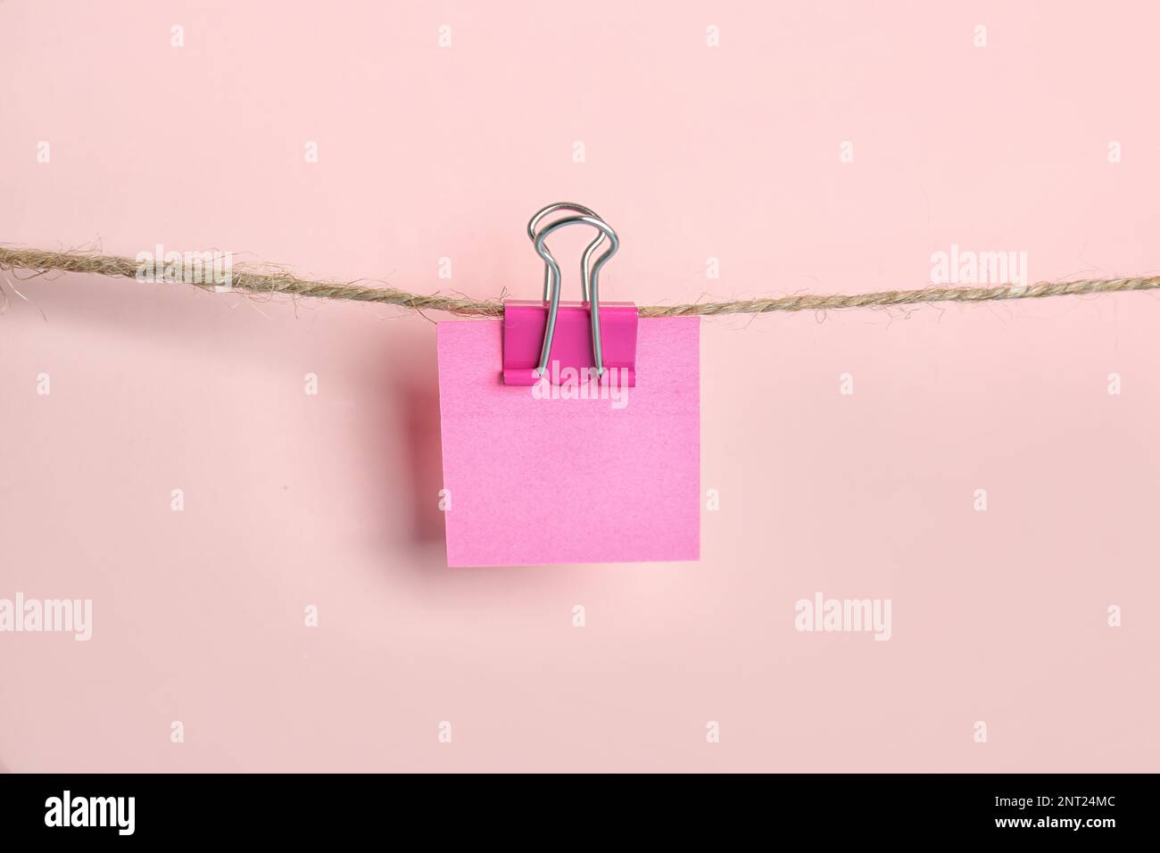 Sticky note with binder clip hanging on rope against pink background ...