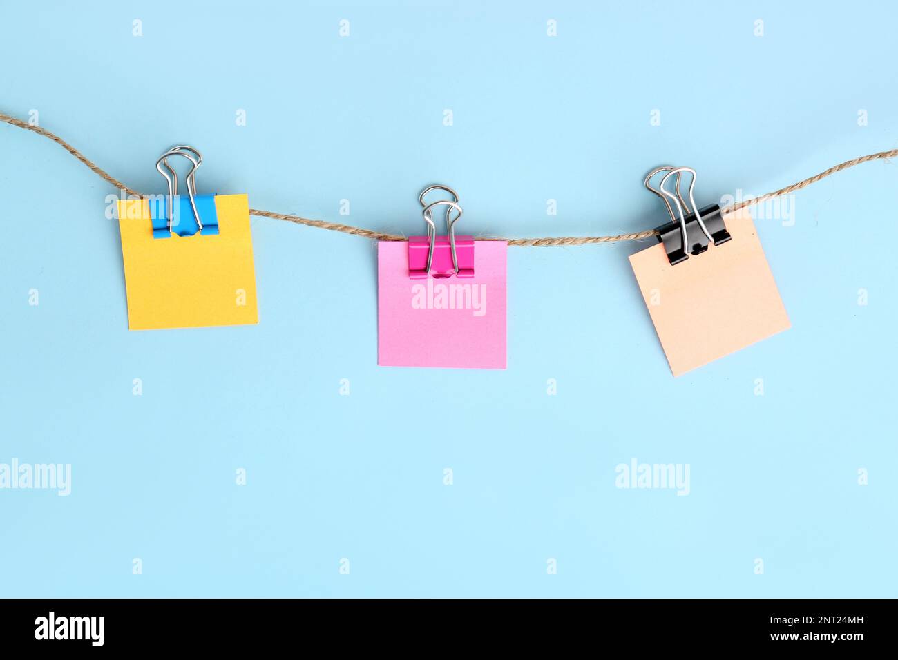 Sticky notes with binder clips hanging on rope against color background ...