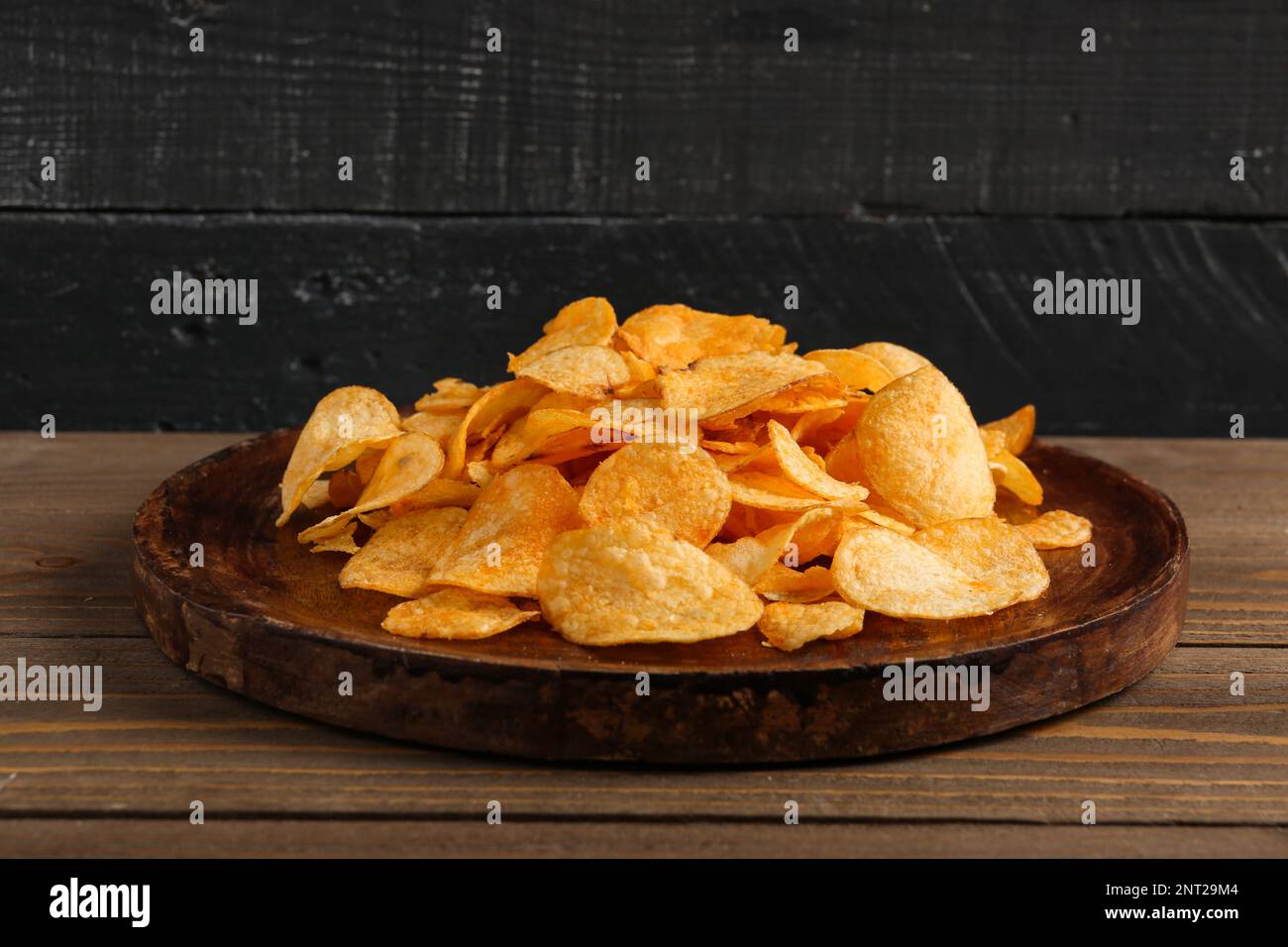 Board with delicious potato chips on brown wooden table against black ...