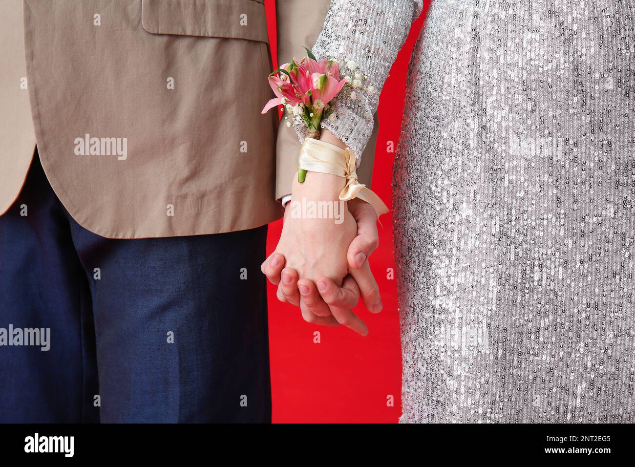 Young girl and her prom date holding hands on red background, closeup ...