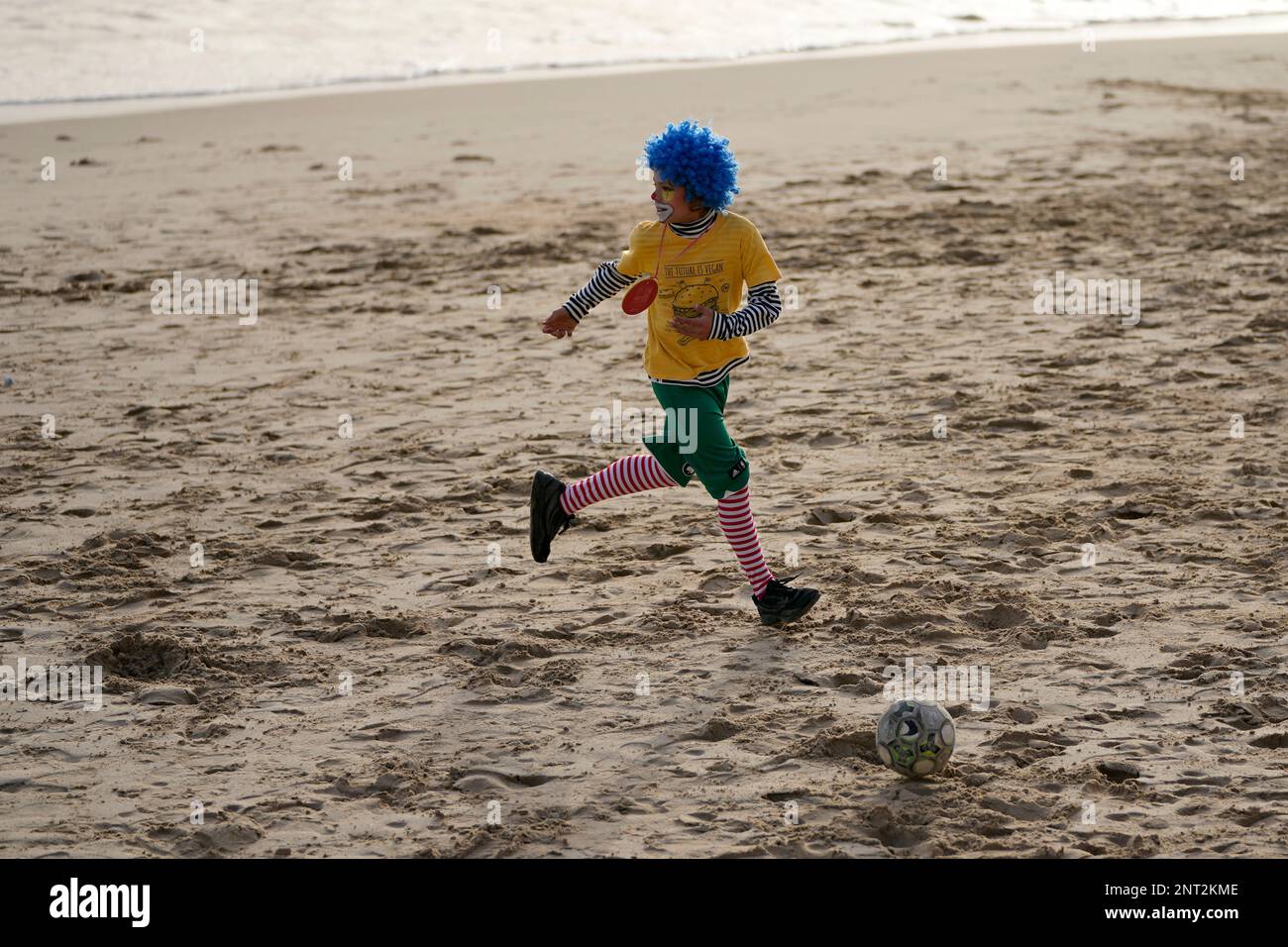 A boy in a clown costume plays with a soccer ball on the beach after ...