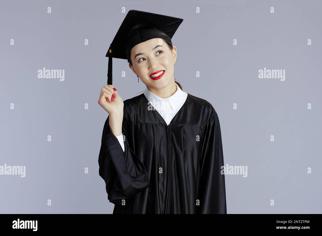 pensive modern graduate student asian woman in graduation gown with cap ...