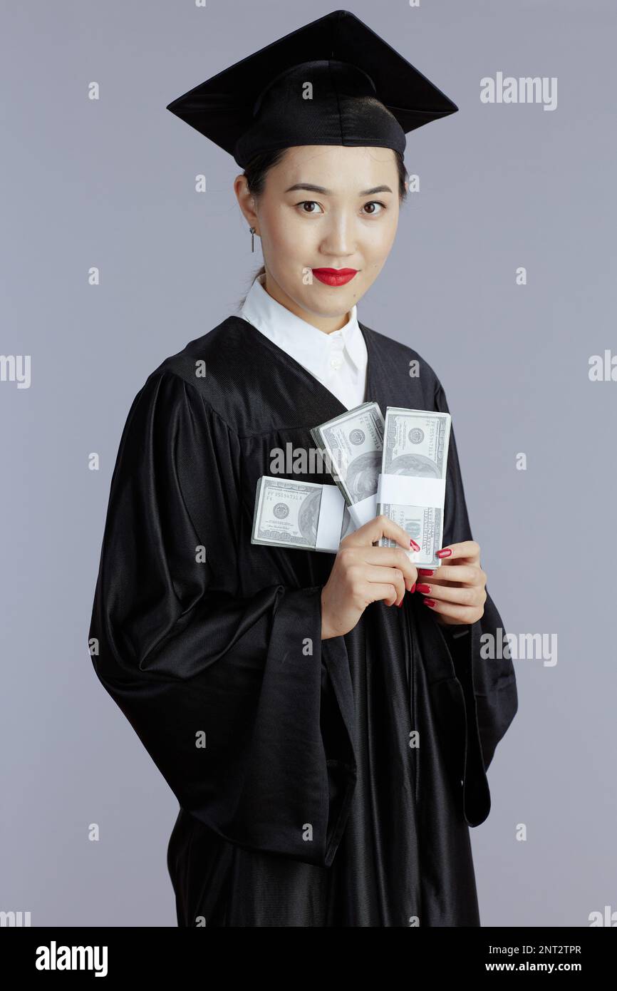 happy modern female asian graduate student with money isolated on gray ...