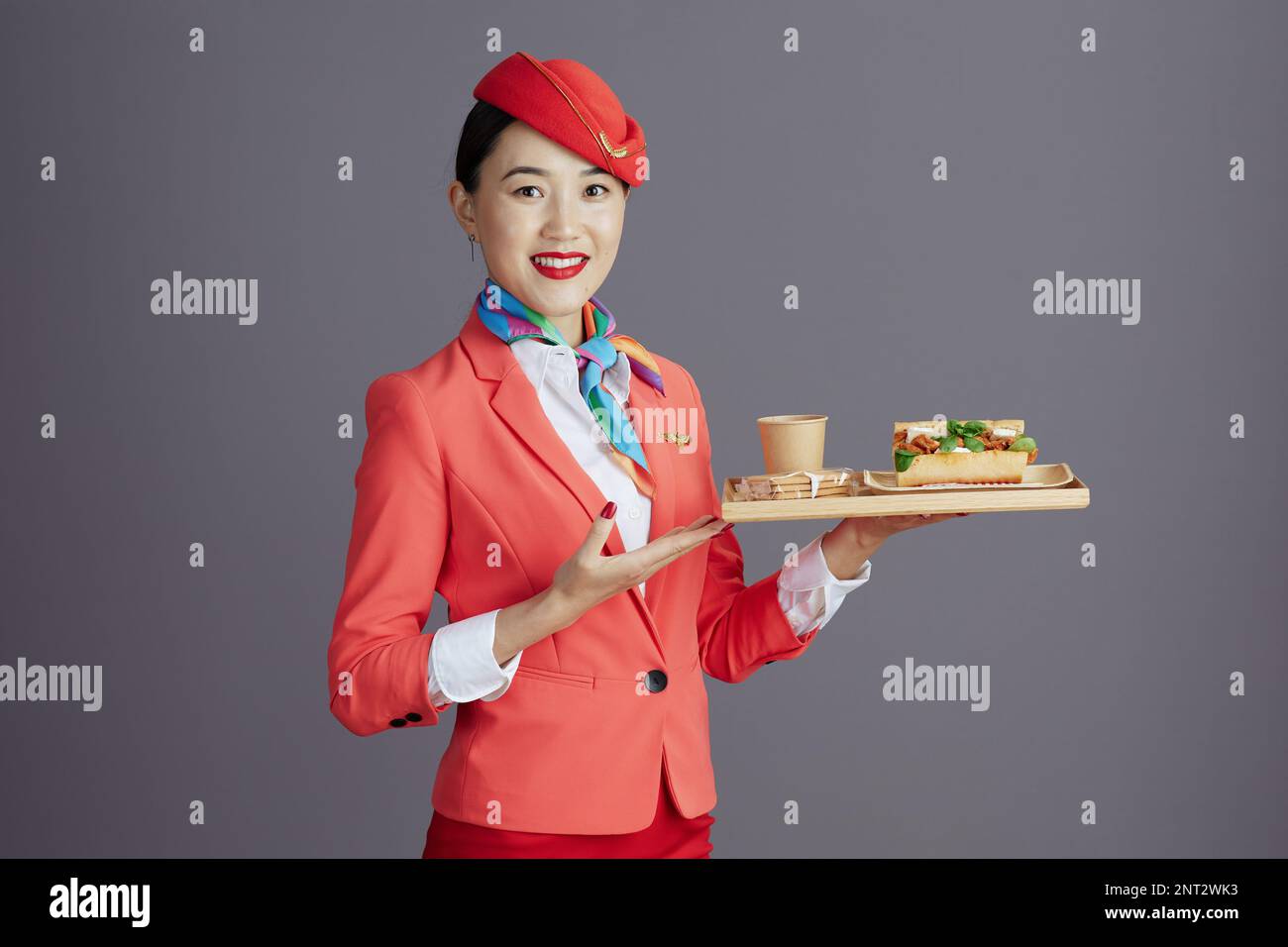 smiling elegant asian female air hostess in red skirt, jacket and hat ...