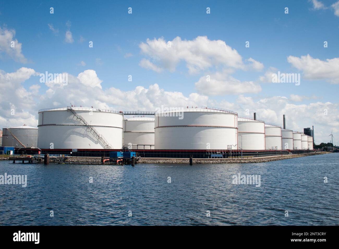 Oil terminal with white oil storage tanks from distance with partially clear sky in background ...