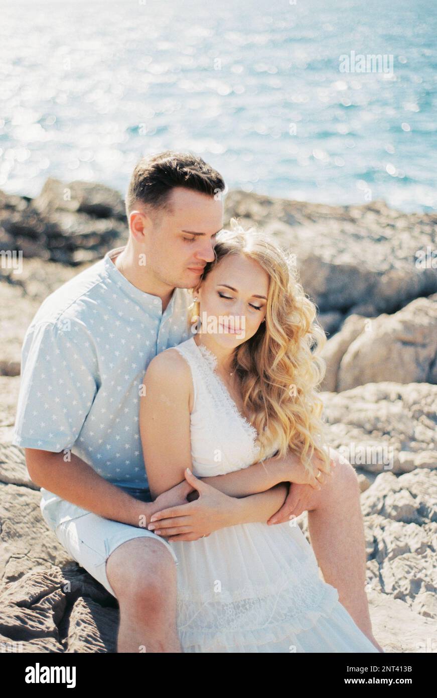 Man hugging a woman sitting on the rocks by the sea Stock Photo - Alamy