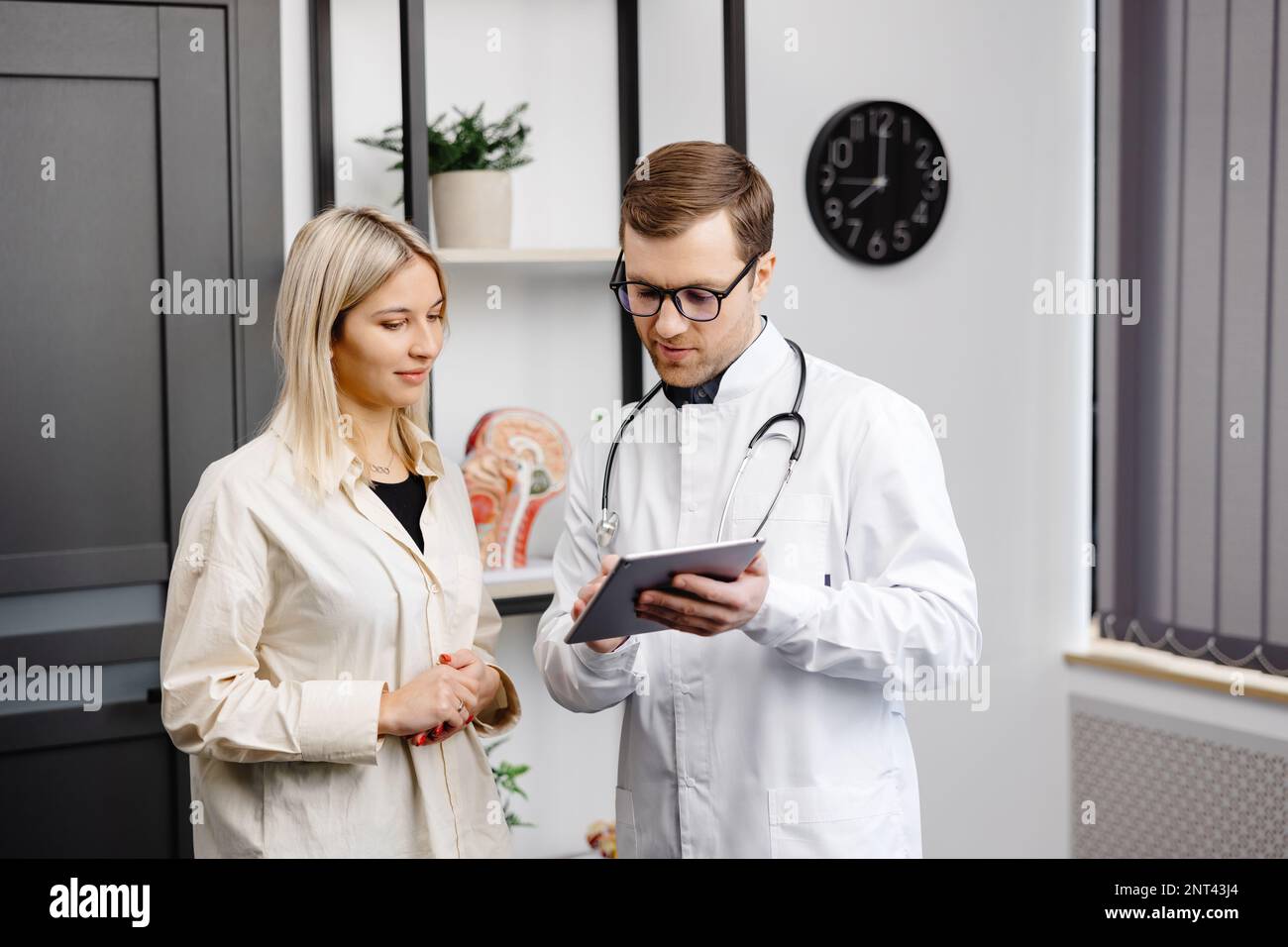 Happy man doctor showing tablet woman patient in clinic office interior ...