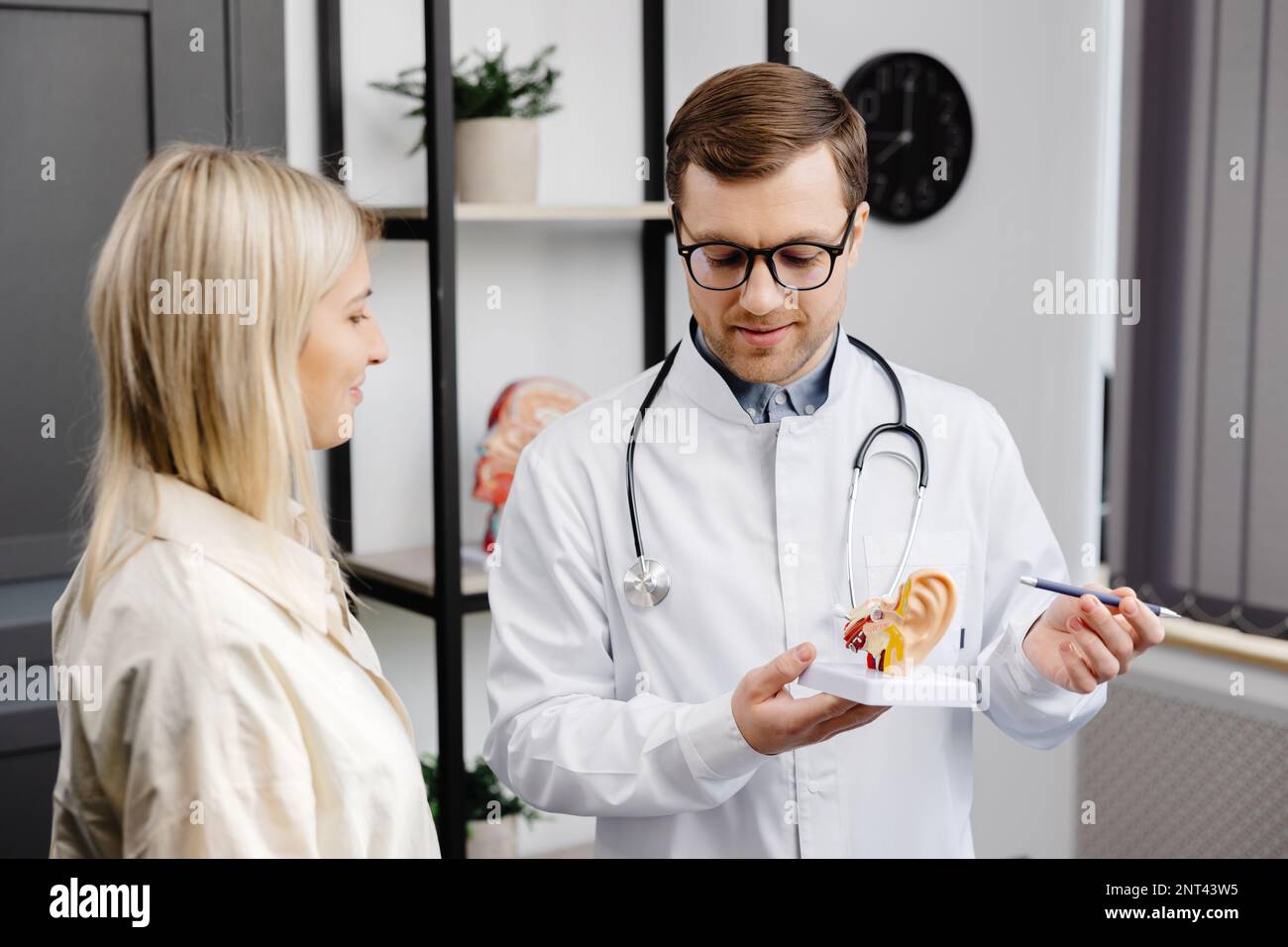 A young attractive otolaryngologist doctor shows a model of the ear and ...