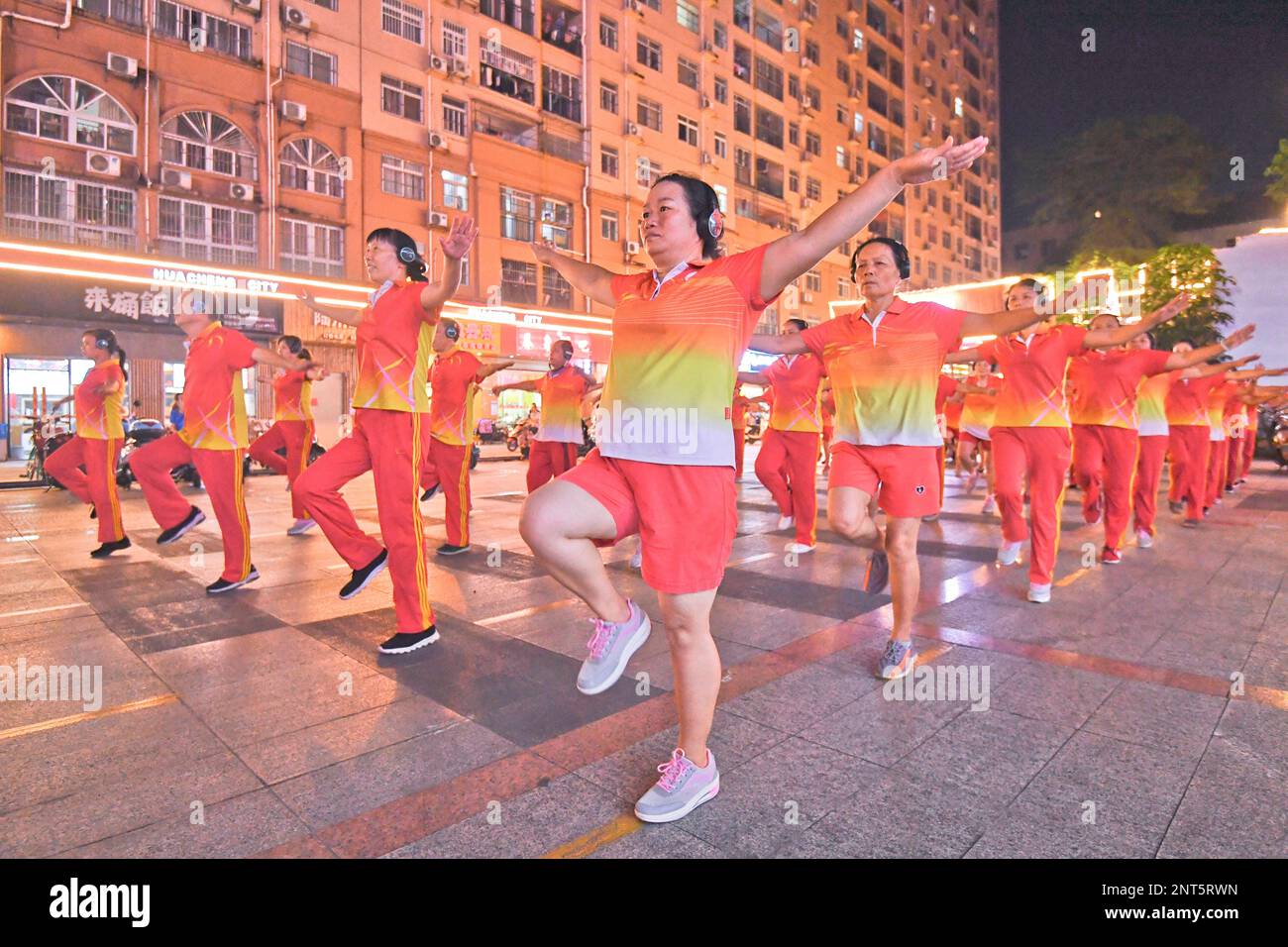 Women wearing headphones exercise in the line dance in a public space ...