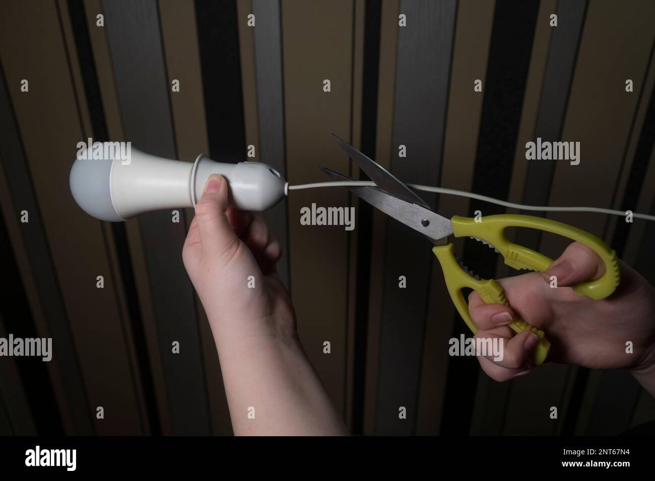 A non-burning electric light bulb in a holder in one hand and scissors ...