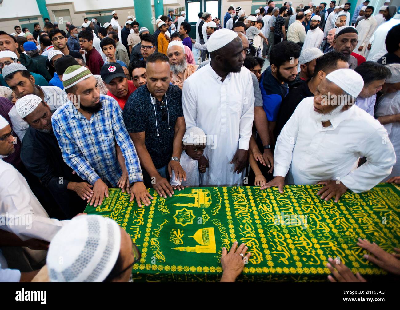 Mourners lay hands on one of the four caskets of the Zaman family ...