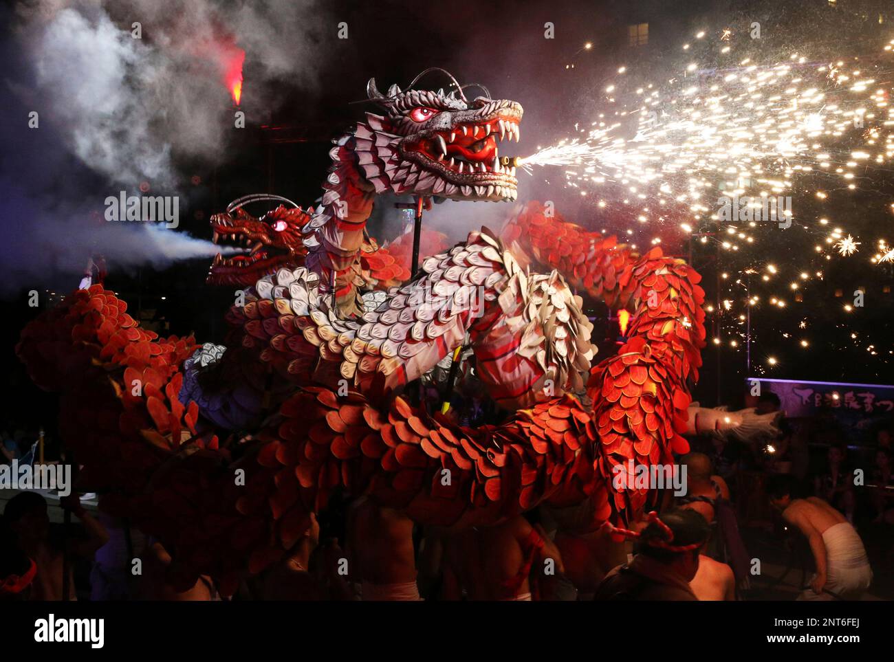 People clad in a loincloth carry a dragon float, portable shrine, and ...